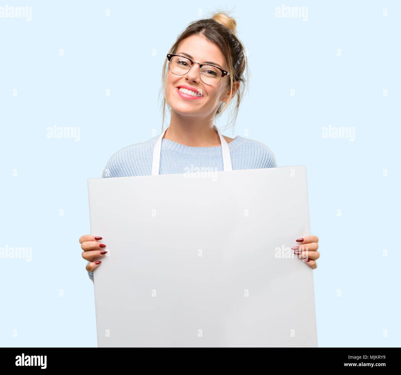 Young woman shop owner, wearing apron holding blank advertising banner ...