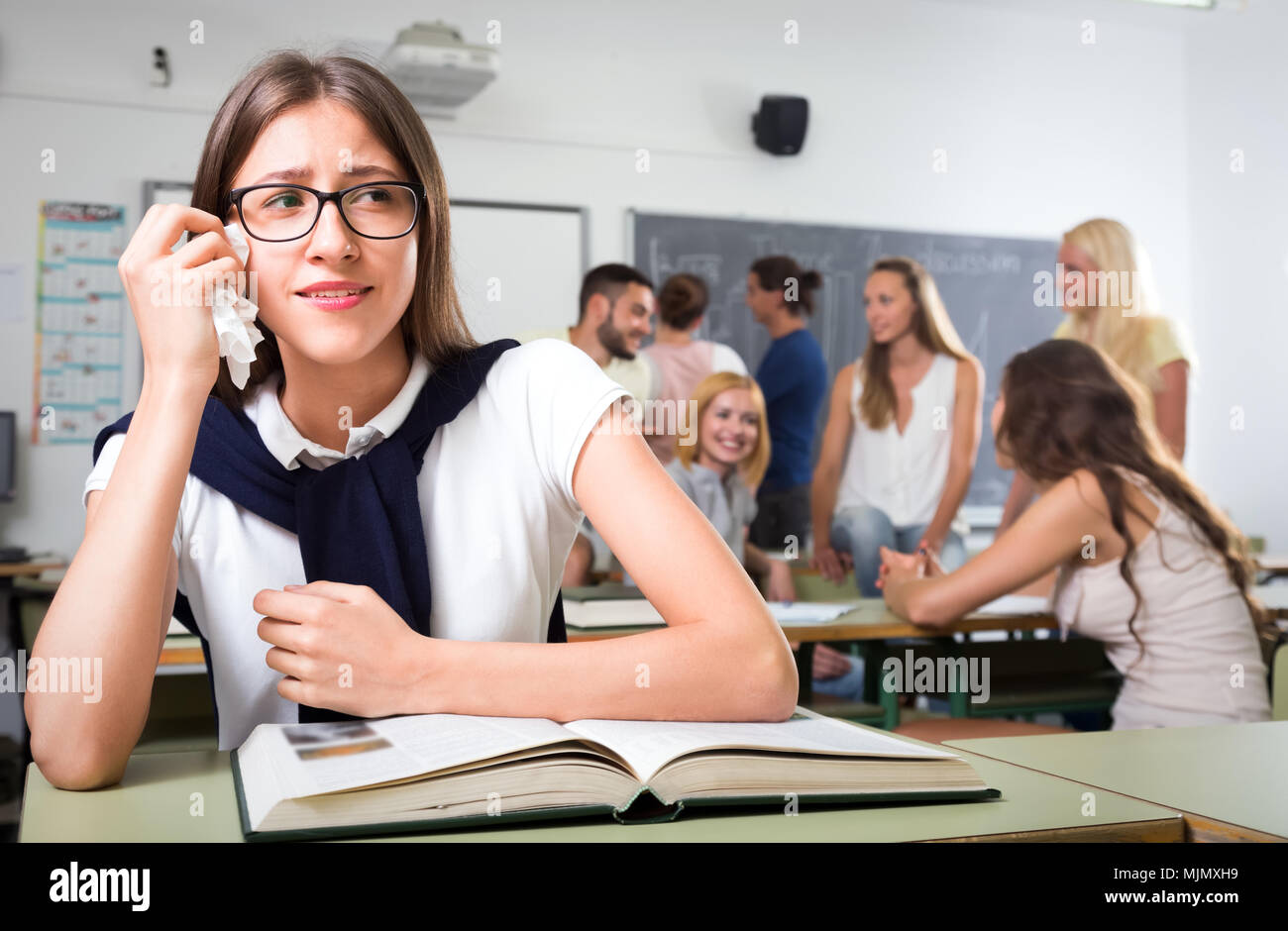 Crying lonely female nerd student sitting at her desk in classroom near ...