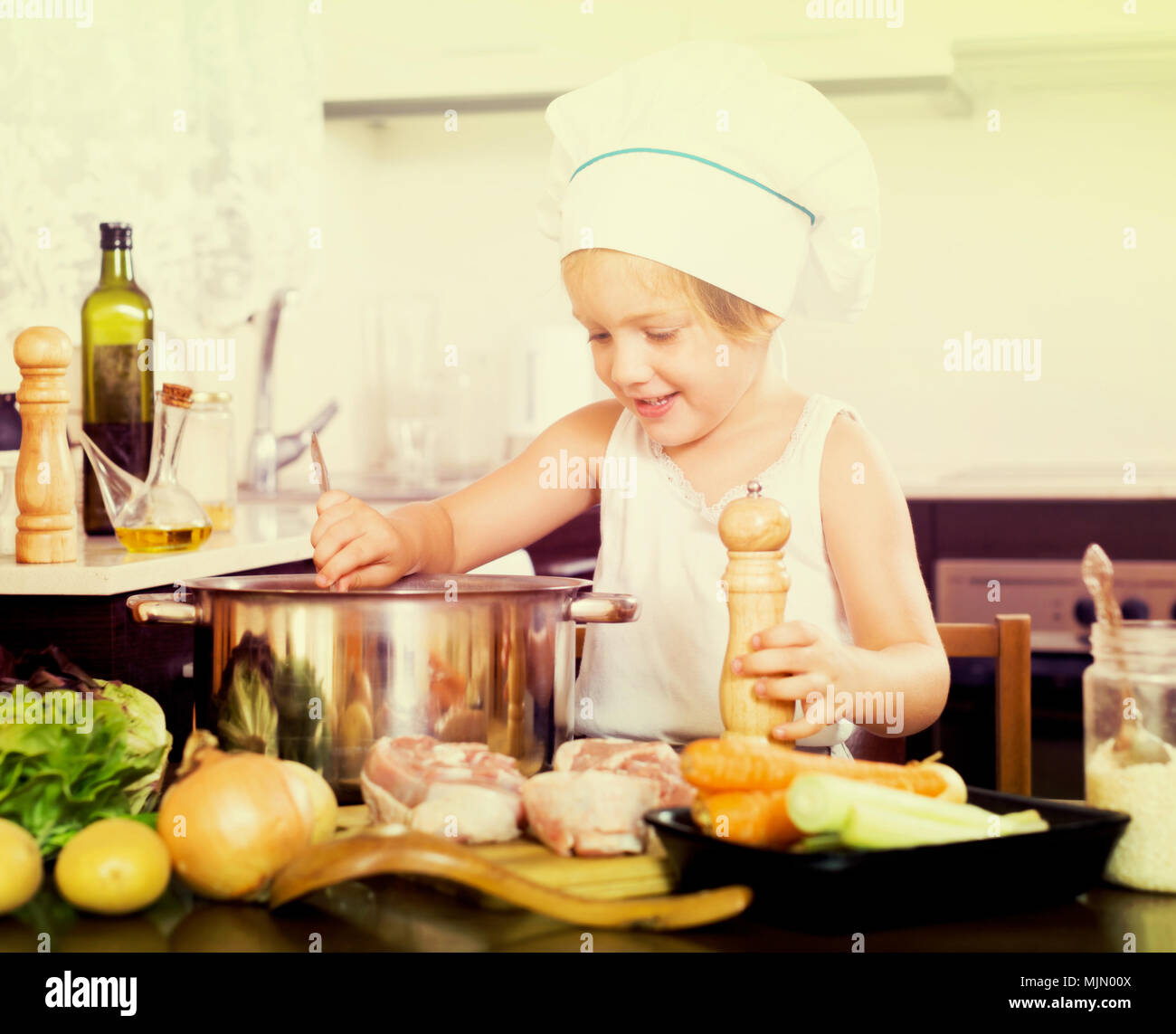 Joyful cute little girl cooking with meat and vegetables at home ...