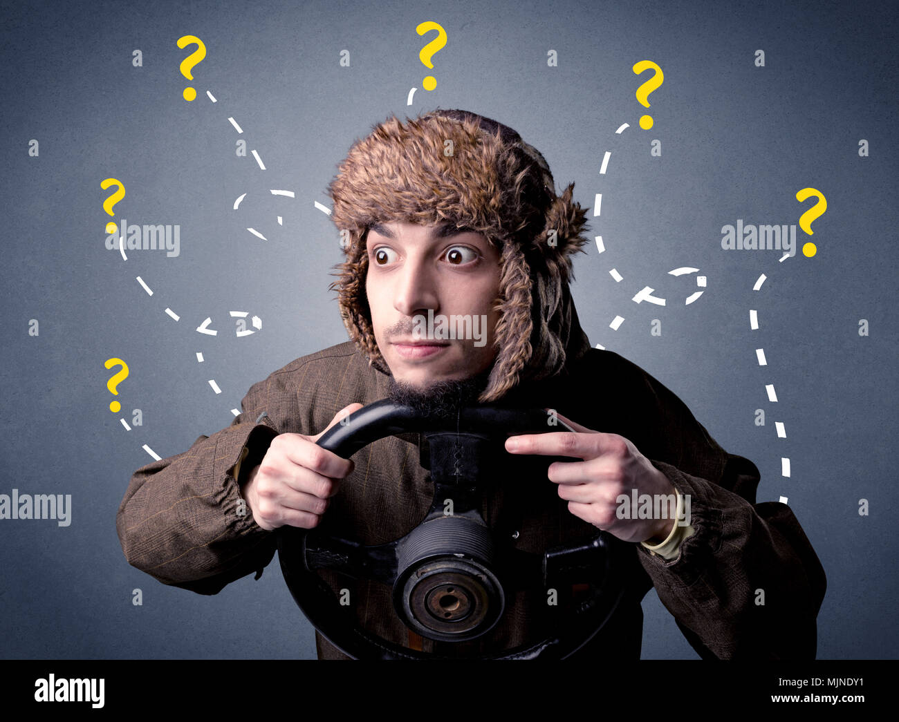 Young man holding black steering wheel with question marks around him ...