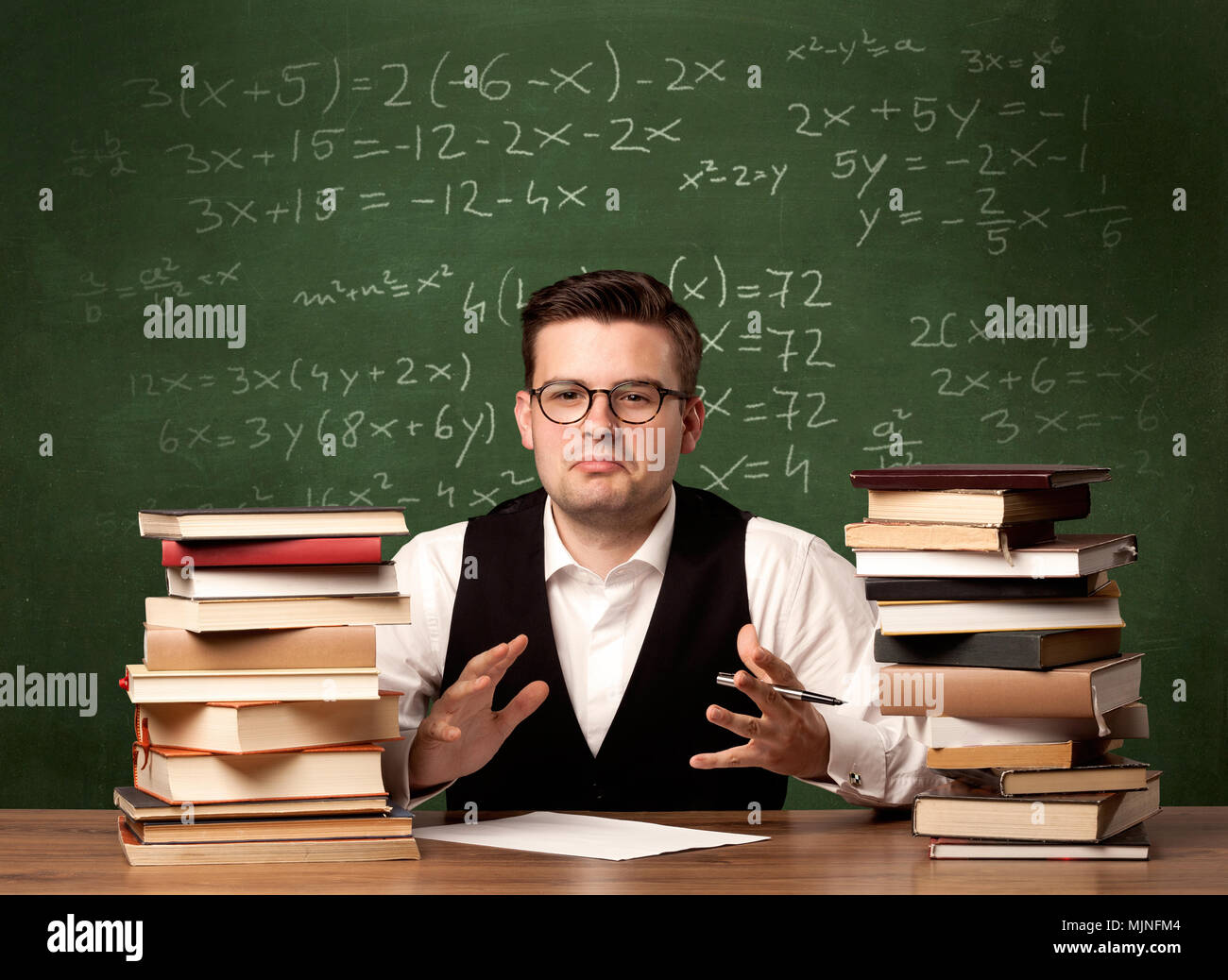 A young ambitious teacher in glasses sitting at classroom desk with ...