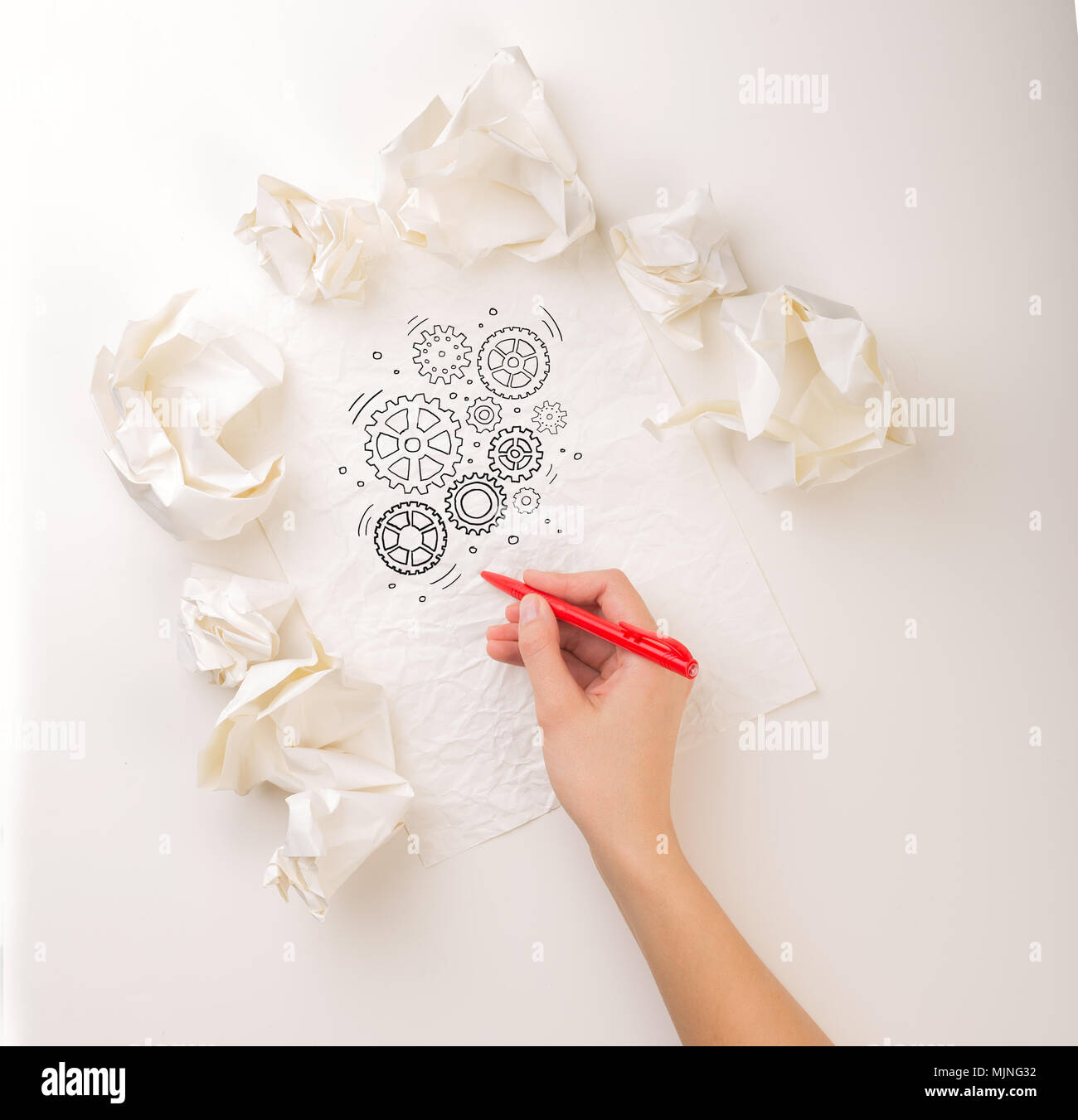 Female hand next to a few crumpled paper balls drawing rotating gears ...