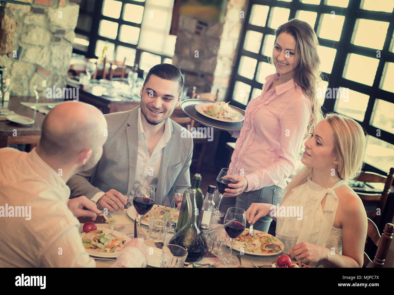 A company of people dining in a restaurant while smiling waitress is ...