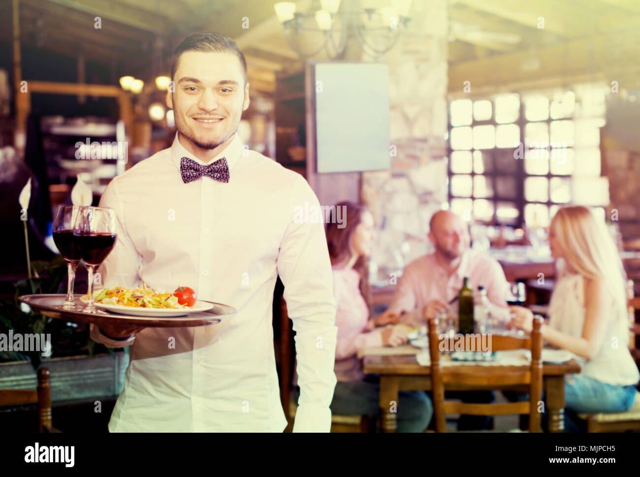 Portrait of a happy male waiter with a tray in his hand at the ...