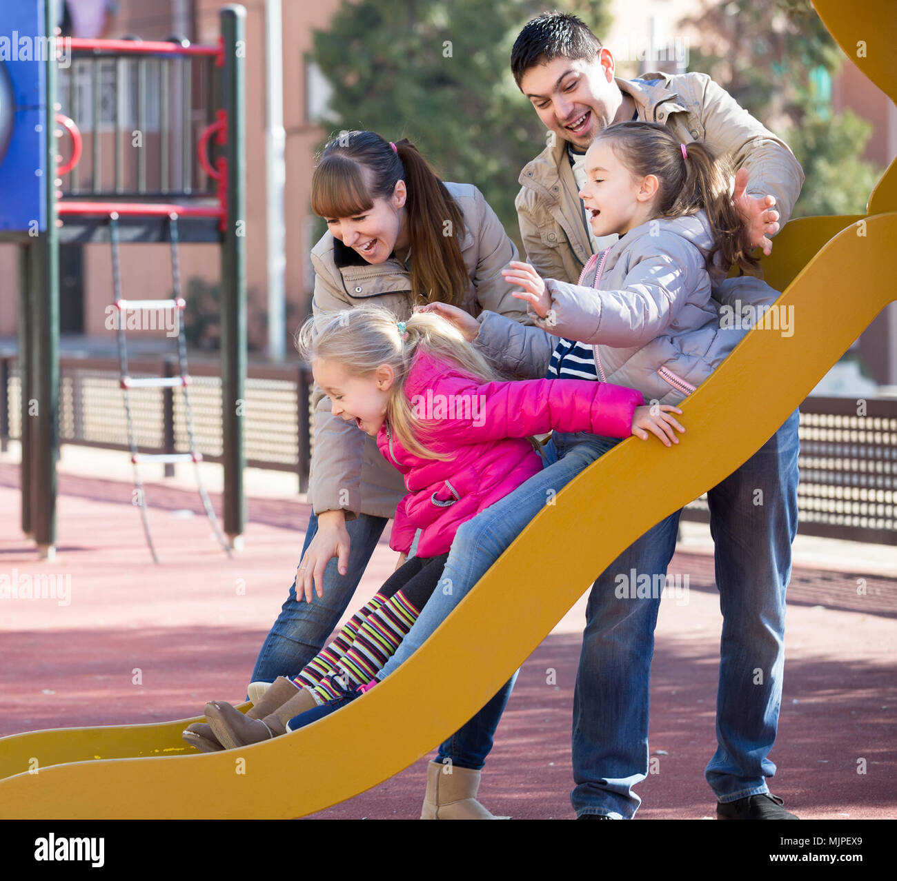 Happy parents playing with little daughters at slide of playground ...