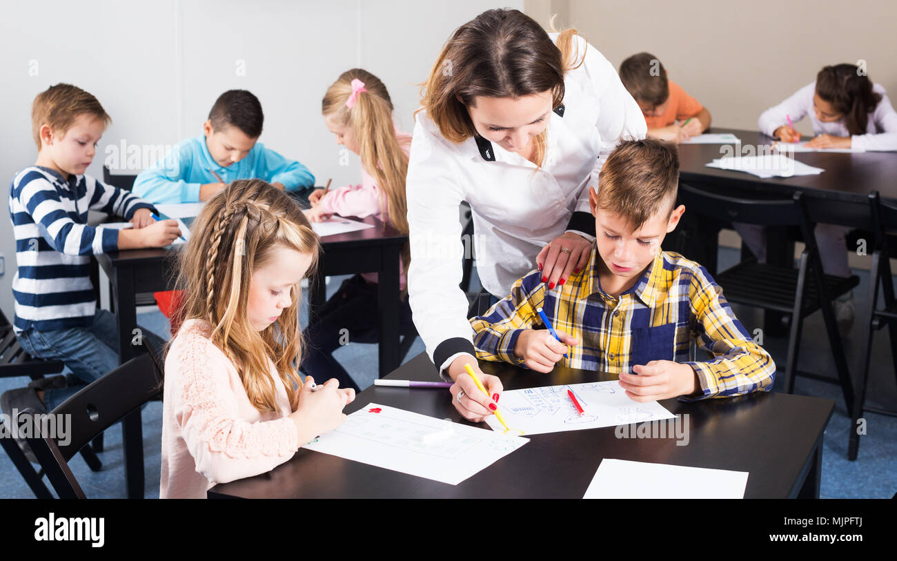 Portrait of positive boys and girls with teacher drawing in classroom ...