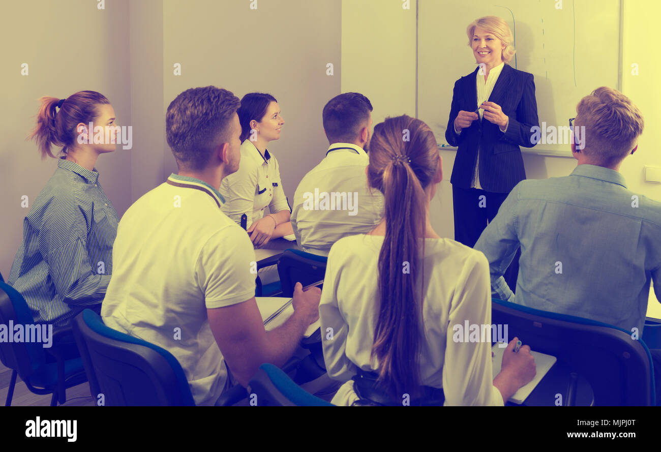 Group of students attentively listening to lecture of female teacher in ...