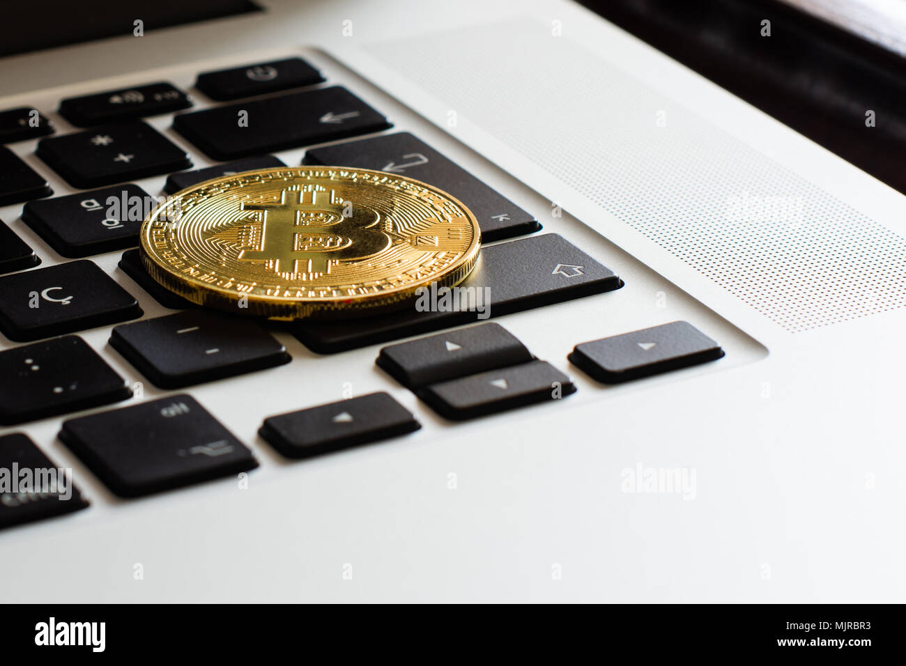 Bitcoin cryptocurrency coin over a laptop's keyboard on a angled view ...
