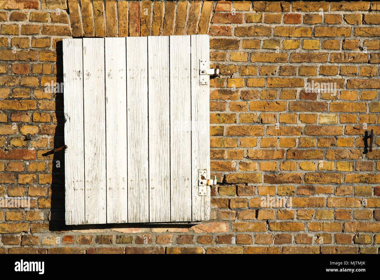 Closed white wooden window hatch with rusted metal hinges on a grungy ...