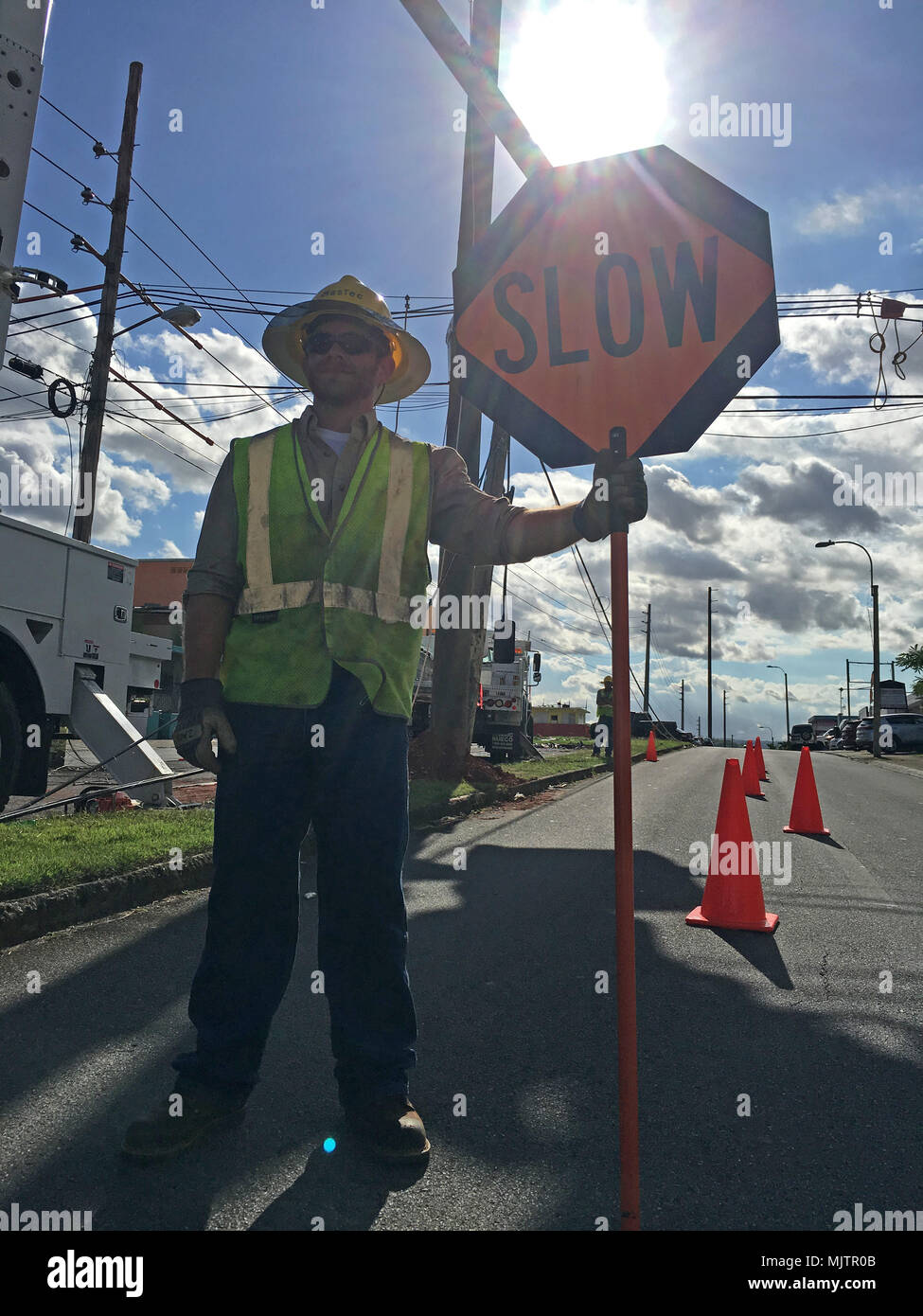 A flagman signals traffic to slow as they pass a crew of linemen from ...