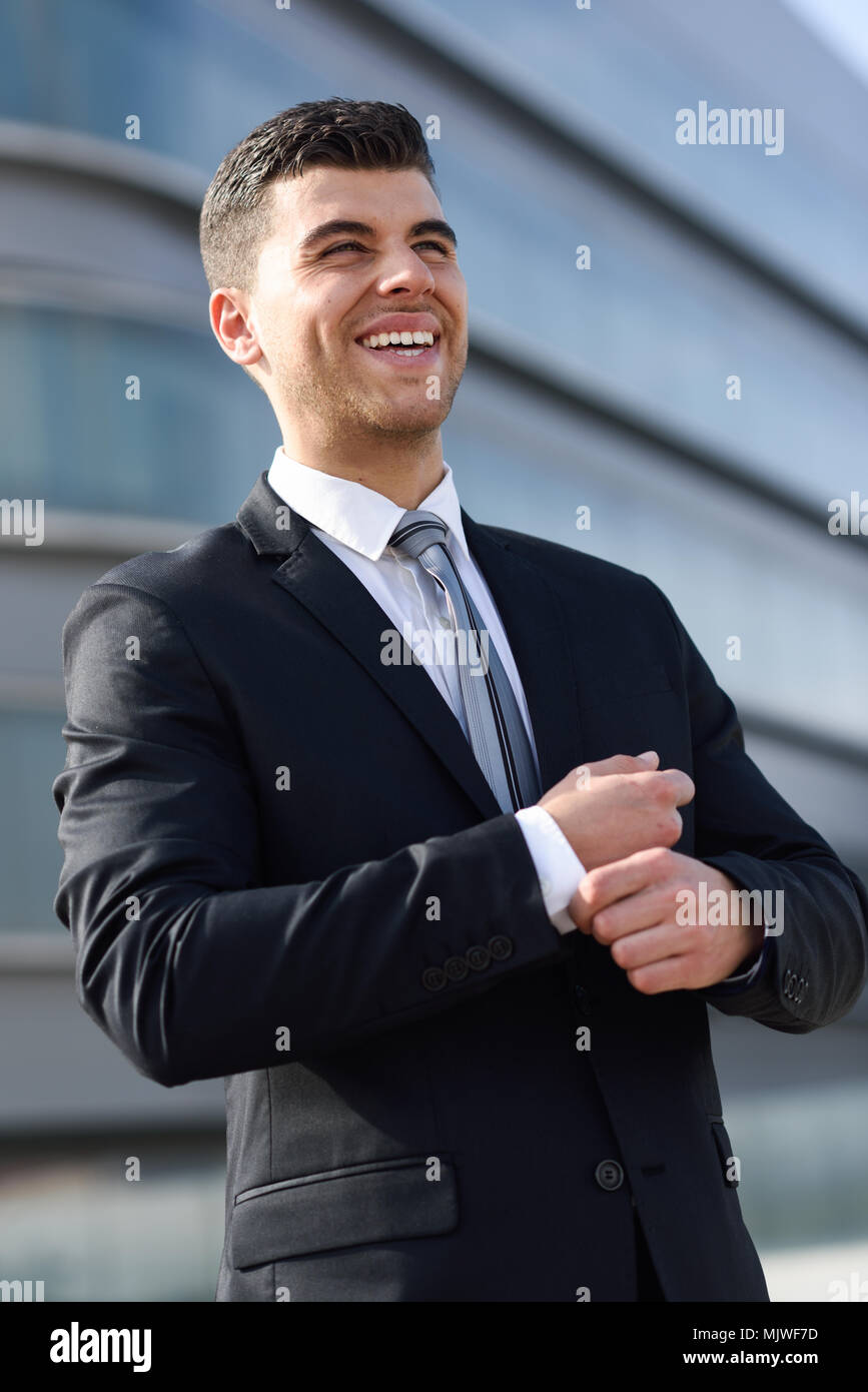 Young businessman near a modern office building wearing black suit and ...