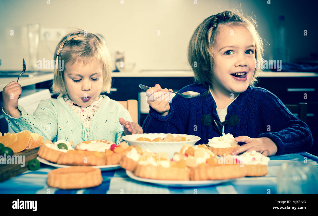 Smiling happy sisters eating delicious cakes with fruits and cream at ...