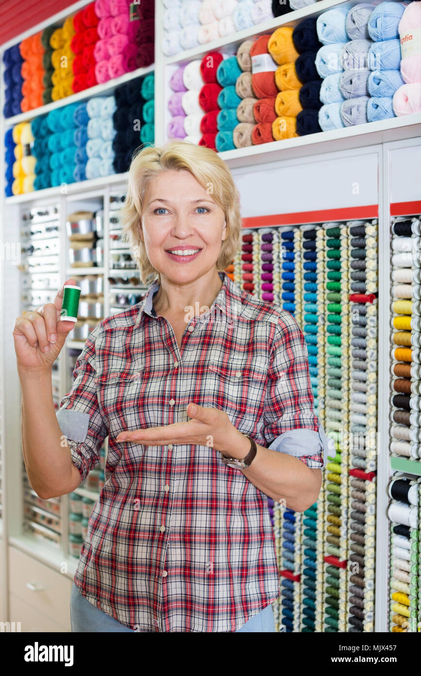 Cheerful mature woman buying colorful thread spools in sewing ...