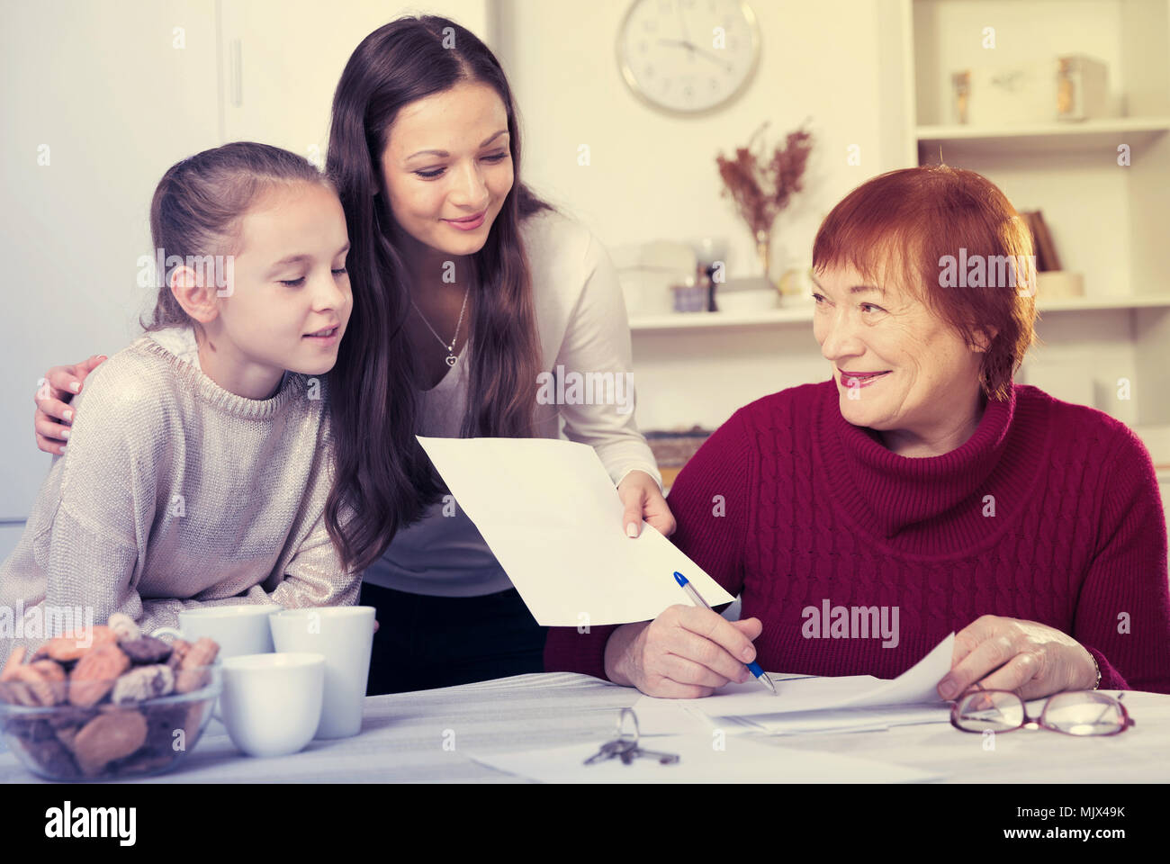 Smiling young woman with little girl helping elderly mother with ...