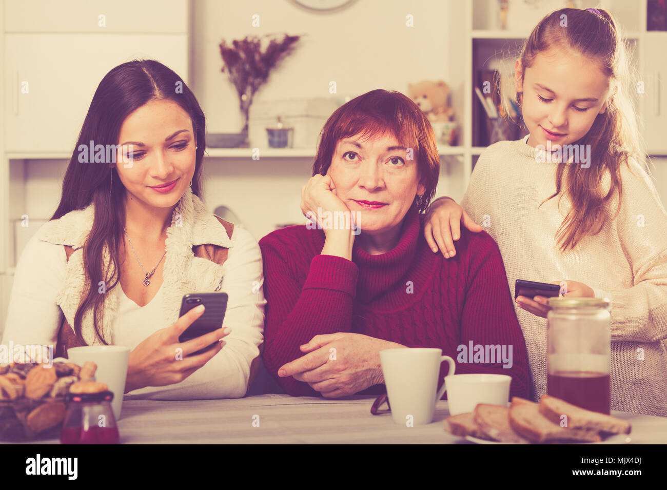 Bored grandma sitting at home table while daughter and granddaughter ...