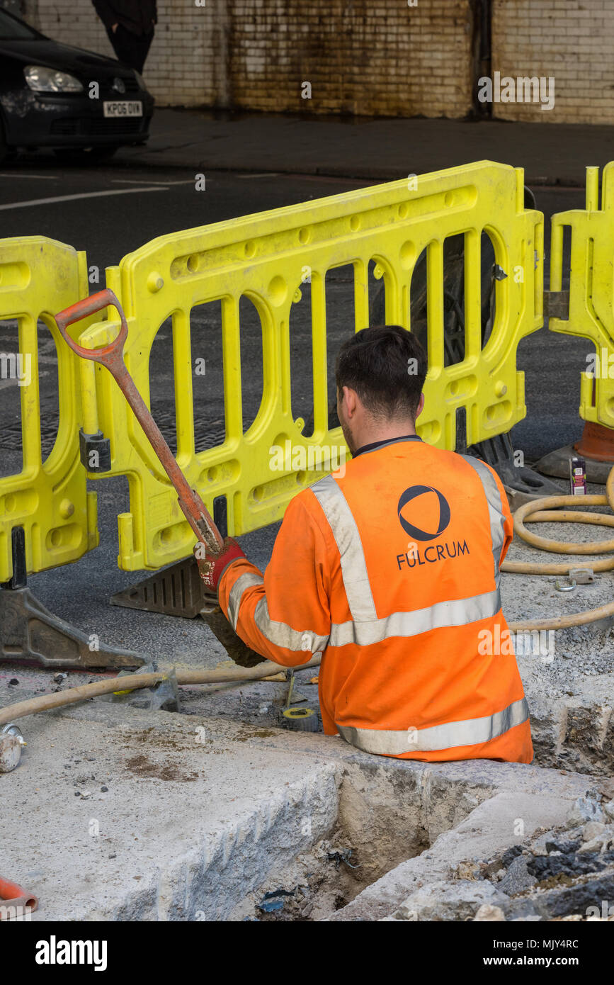 A man wearing high visibility orange clothing working digging a hole in ...