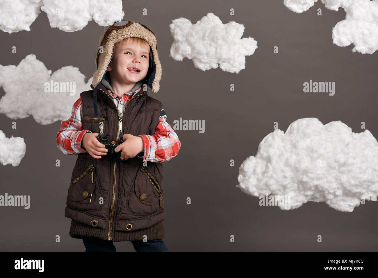 boy dressed as an airplane pilot stands between the clouds and looks ...