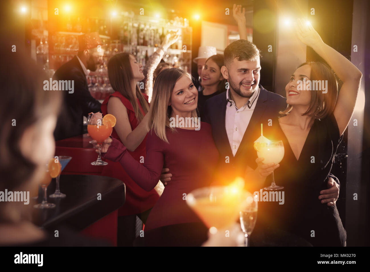 Cheerful guy with two girls partying in bar, dancing and toasting ...