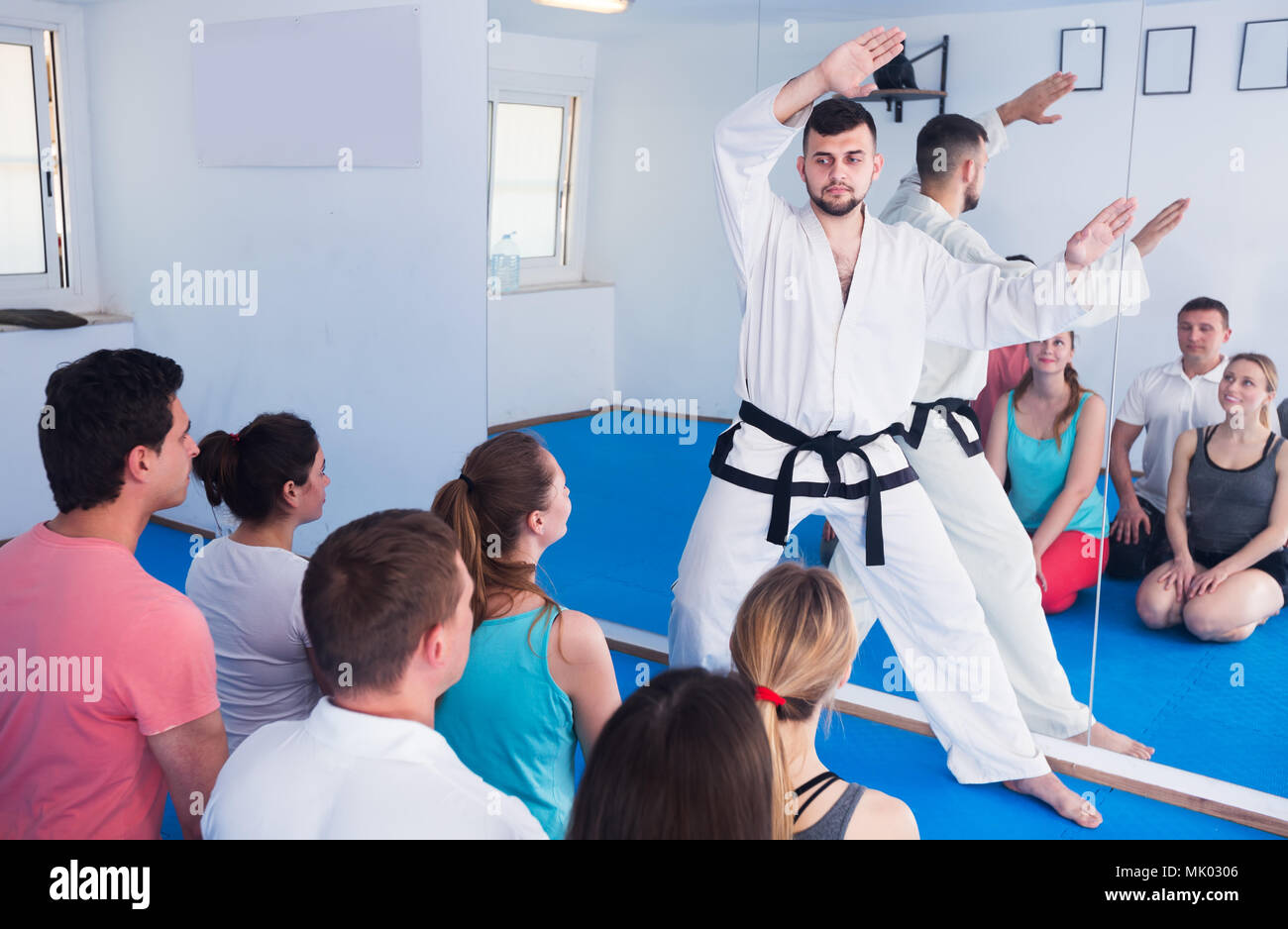 Young male trainer demonstrating new techniques to adults in karate ...