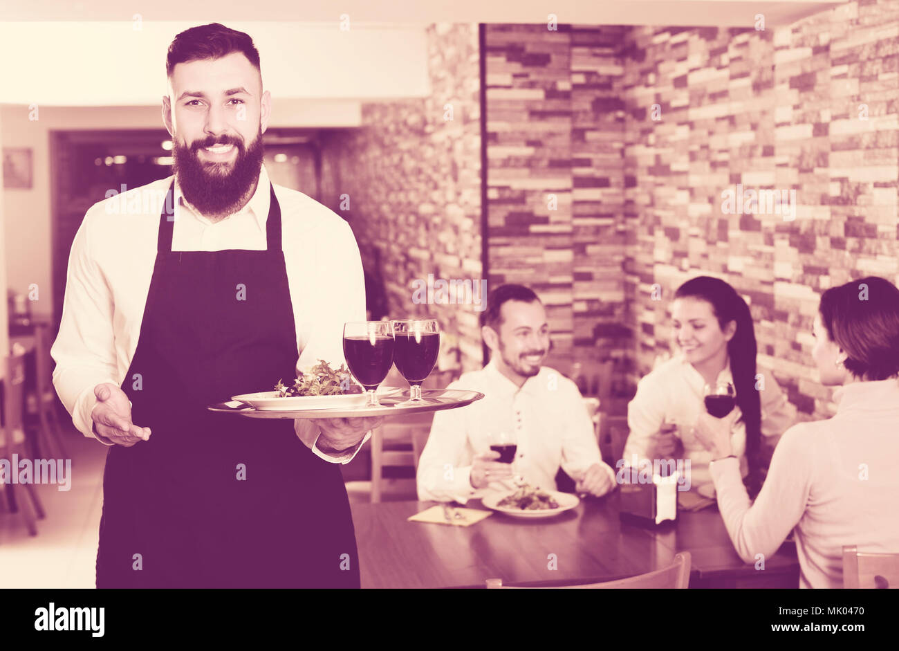 Positive male waiter welcoming guests to country restaurant Stock Photo ...