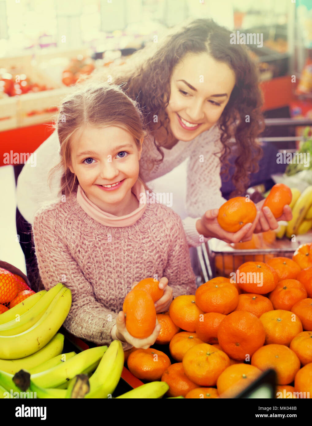 Happy mother and small cheerful daughter buying sweet citrus fruits ...
