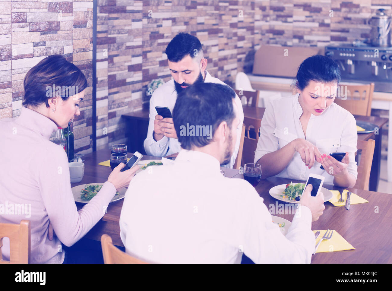 group of concentrated friends busy with phone ignoring dinner in ...