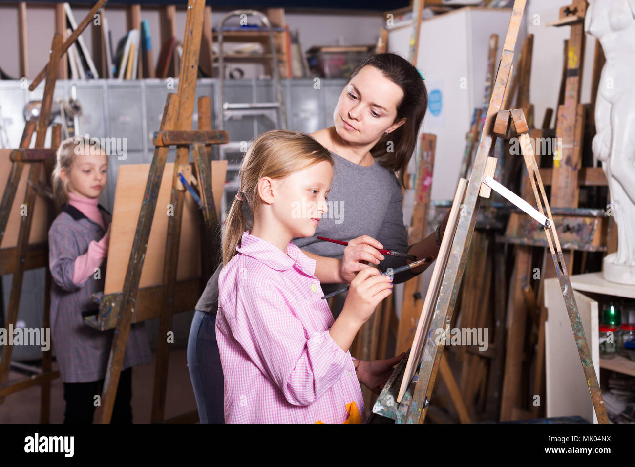Skillful woman teacher correcting work of girl during painting class at ...