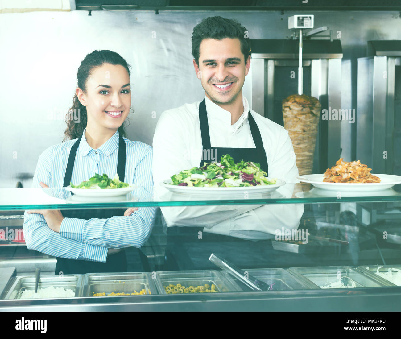 Positive adult restaurant staff posing at kebab counter and smiling ...