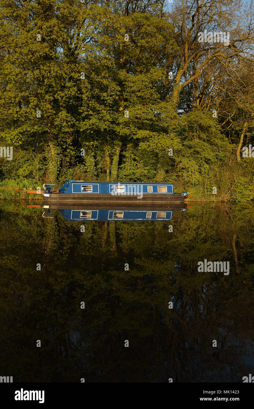 Canal barge narrow boat reflected in water surrounded by trees in late ...