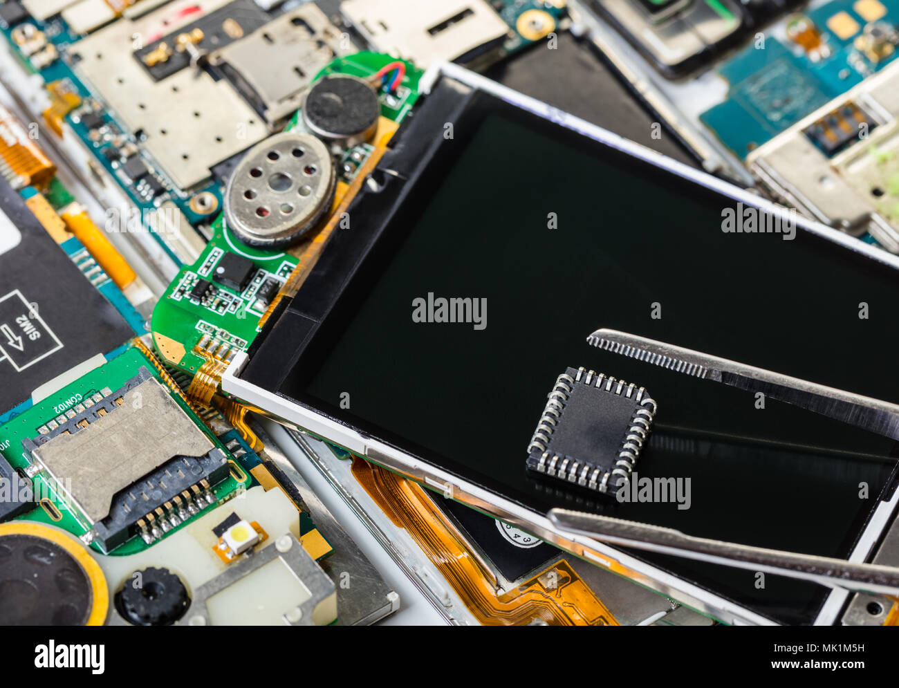 electronic chip and tweezers on background of the disassembled mobile ...