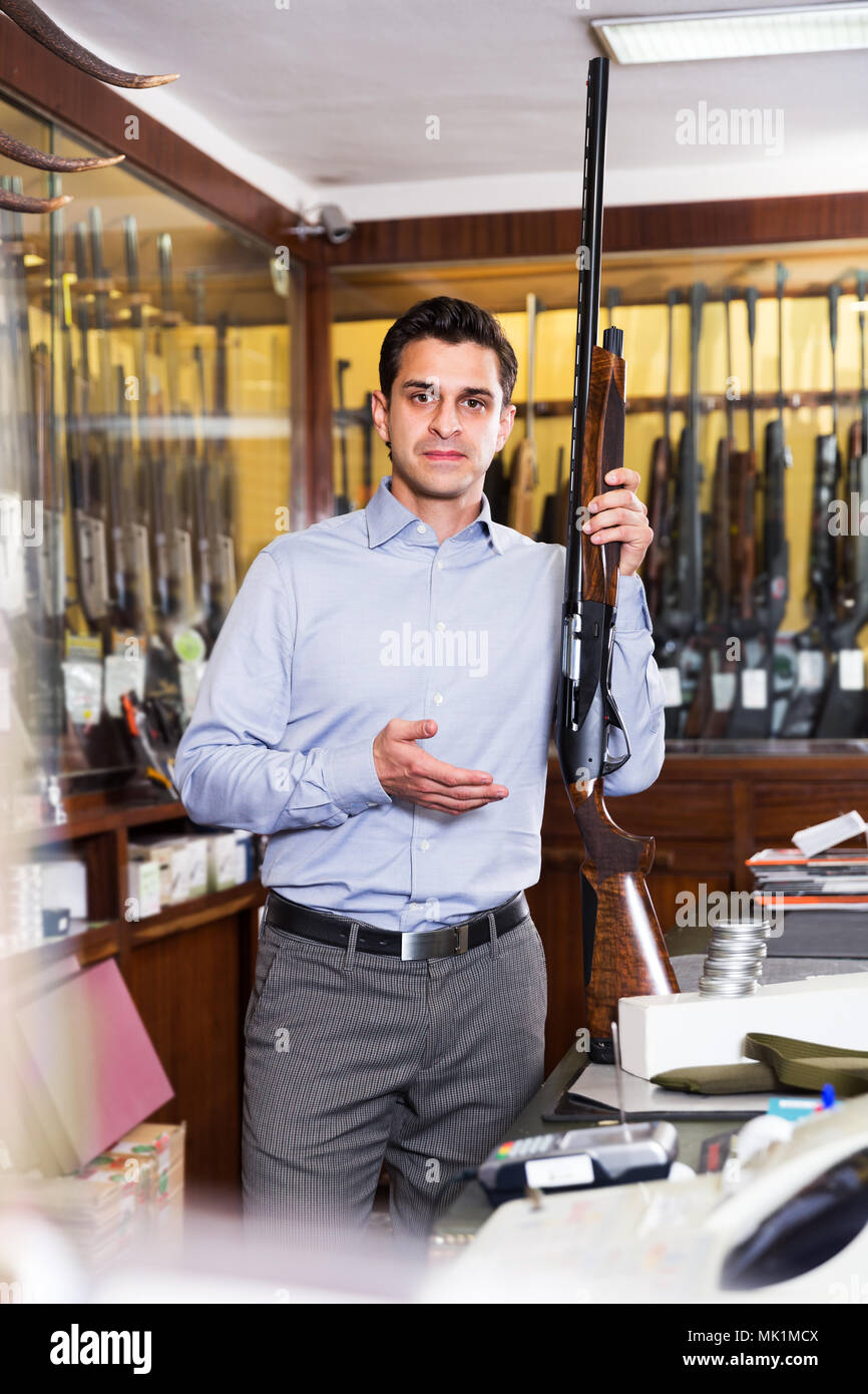 Portrait of positive salesman in gun store showing rifle Stock Photo ...