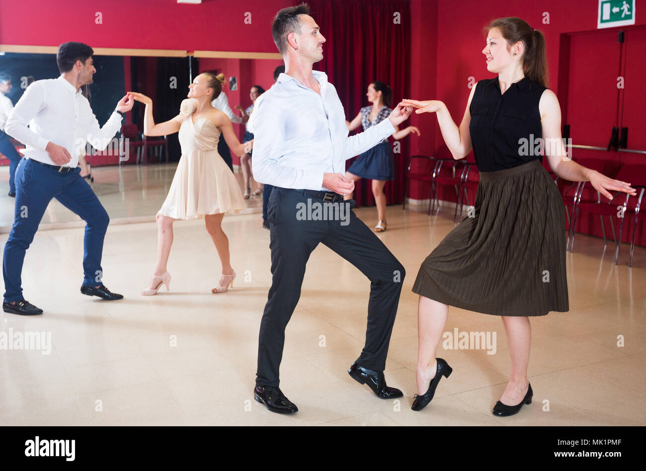 Young smiling people practicing vigorous twist movements in dance class ...