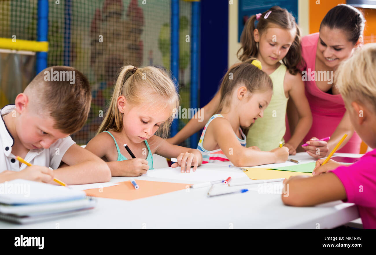 Happy children drawing on lesson in elementary education class with help of teacher Stock Photo ...