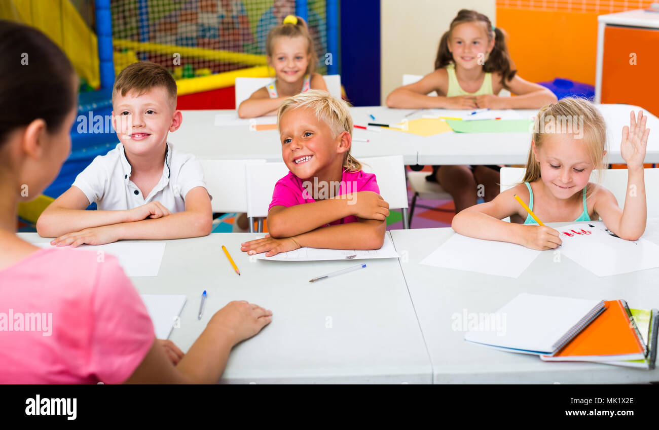 joyful primary school kids sitting at the desks and doing exercises at ...