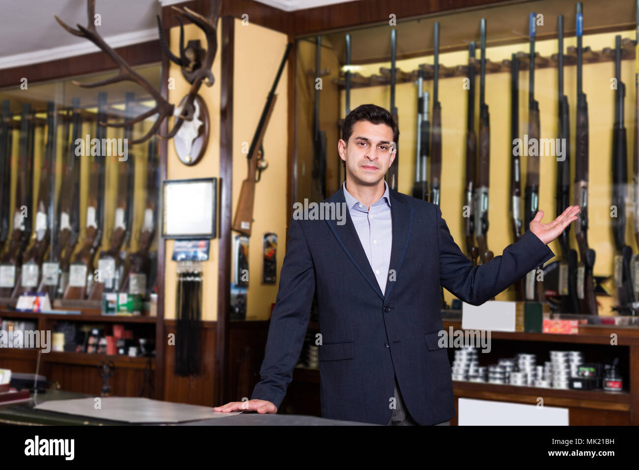Portrait of male owner of hunting shop showing showcase with rifles ...