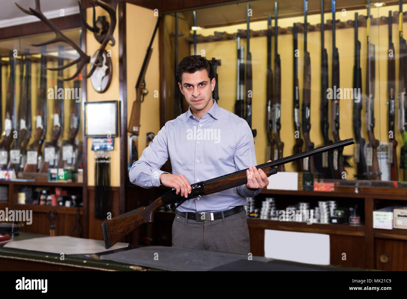Portrait of adult male owner of hunting shop standing with shotgun ...