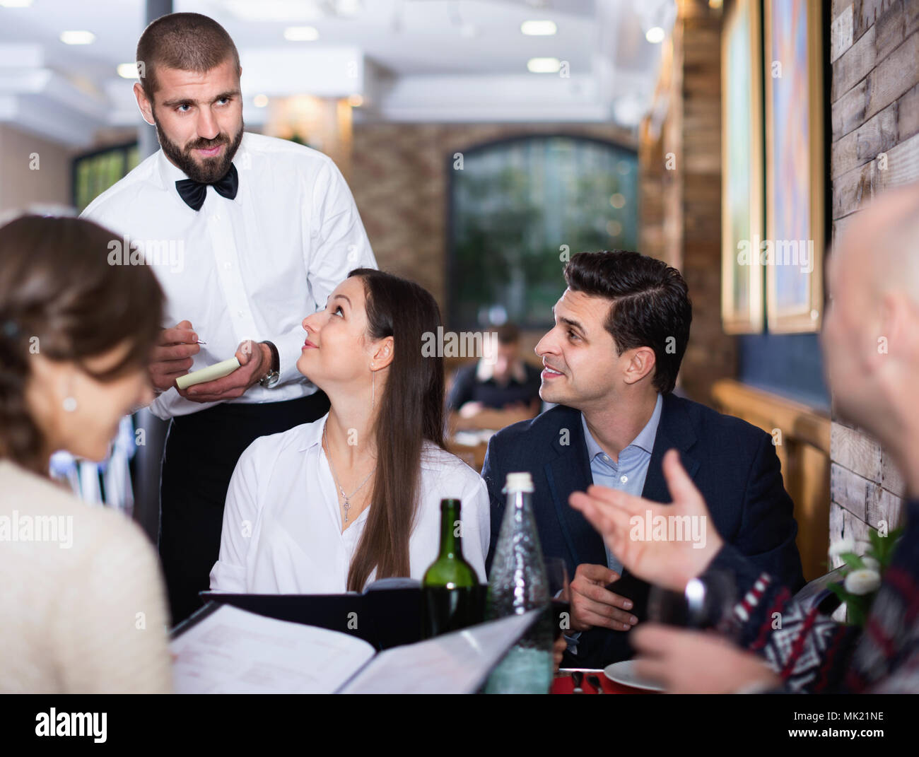 Diligent pleasant waiter with notebook taking order from friendly ...