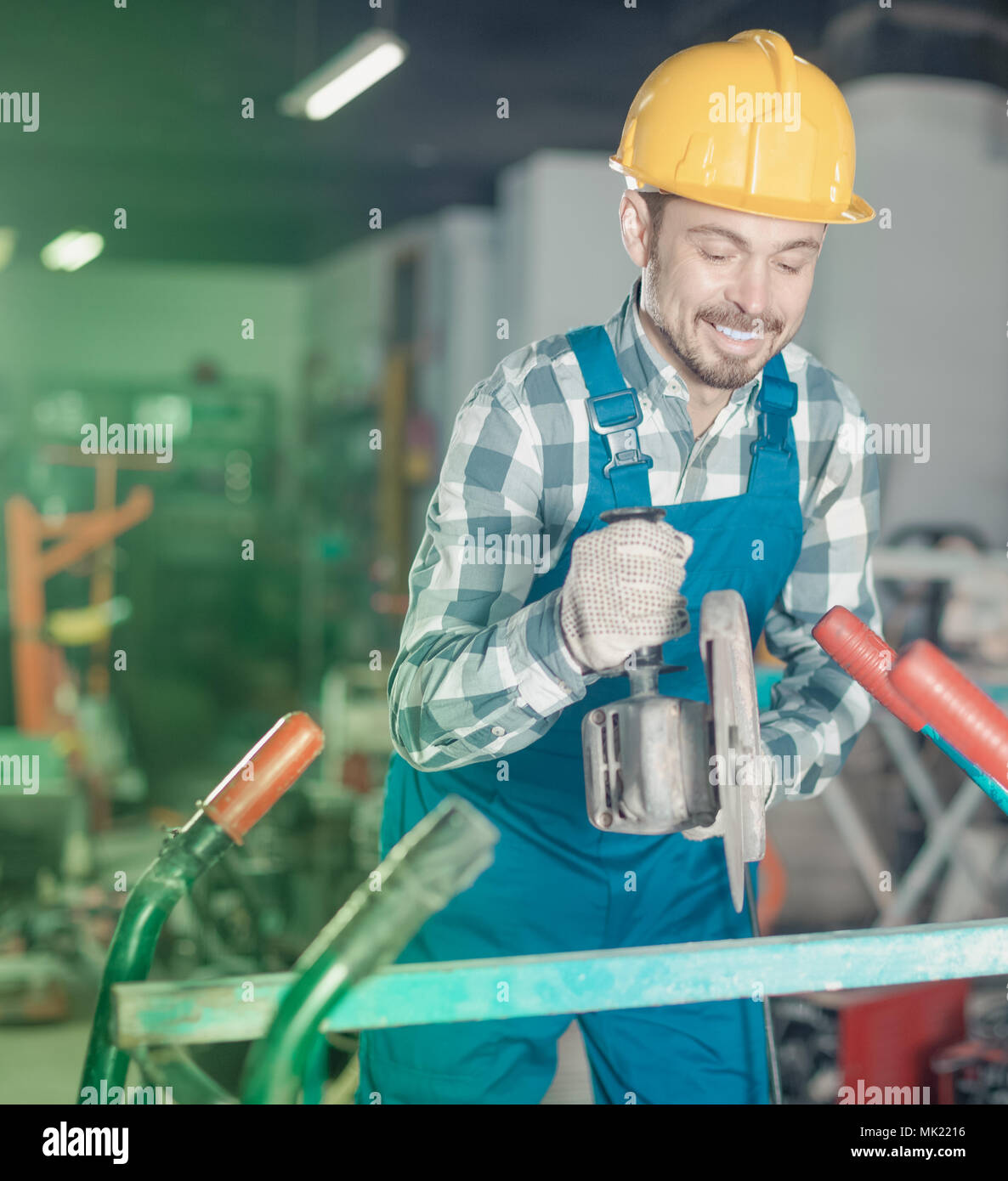 Young smiling guy using angle grinder for construction work at workshop ...