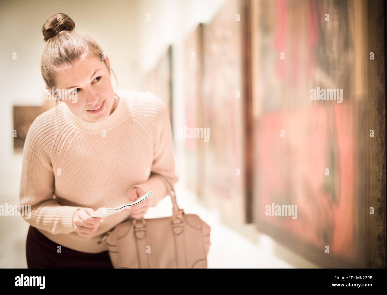 Portrait of young woman with the guide looking at pictures at a museum ...