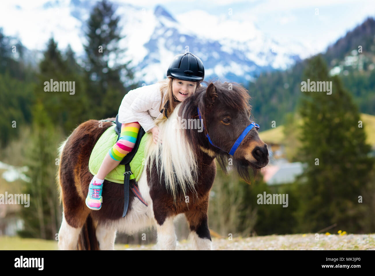 Kids riding pony in the Alps mountains. Family spring vacation on horse ...
