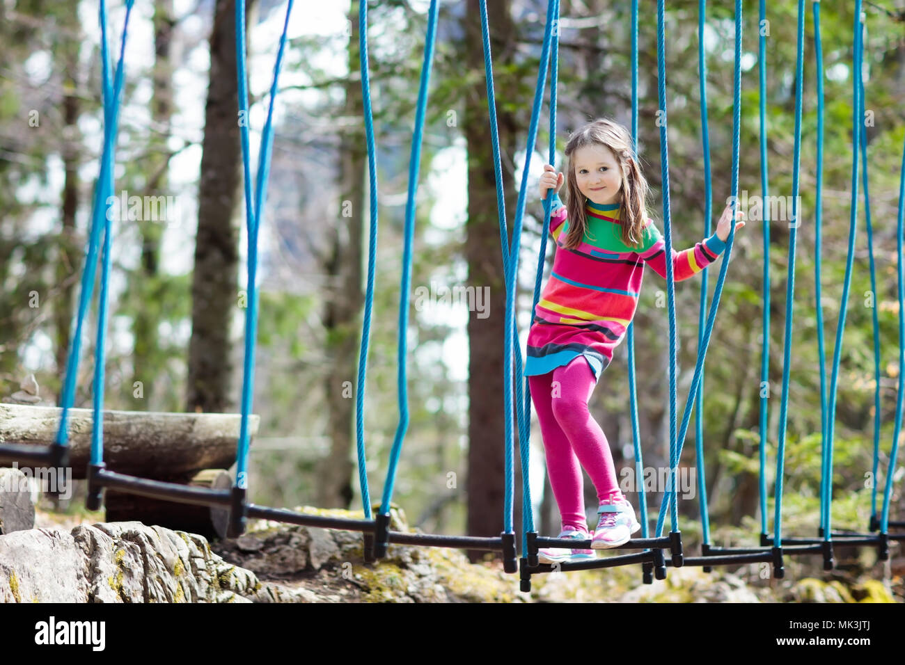 Child in forest adventure park. Kids climb on high rope trail. Agility ...
