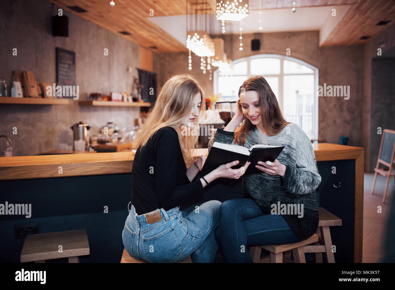 Two Girl`s absorbed in reading book during the break in cafe. Cute ...