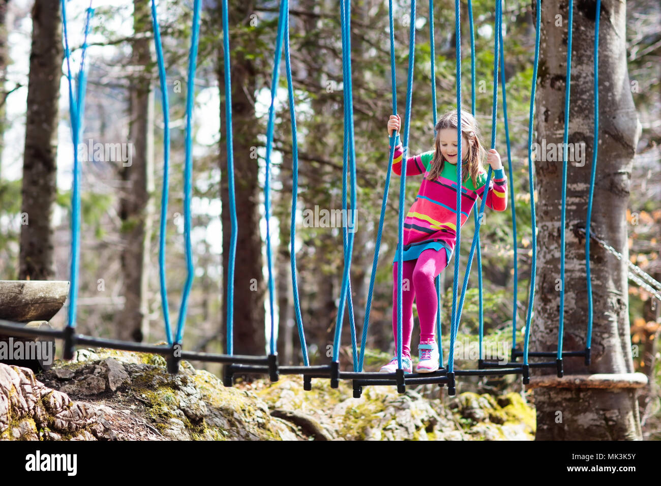 Child in forest adventure park. Kids climb on high rope trail. Agility ...