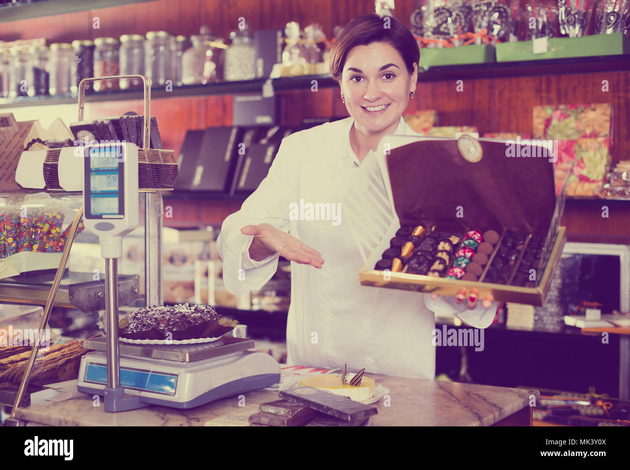 Young shop assistant demonstrating box of delicious chocolates in ...