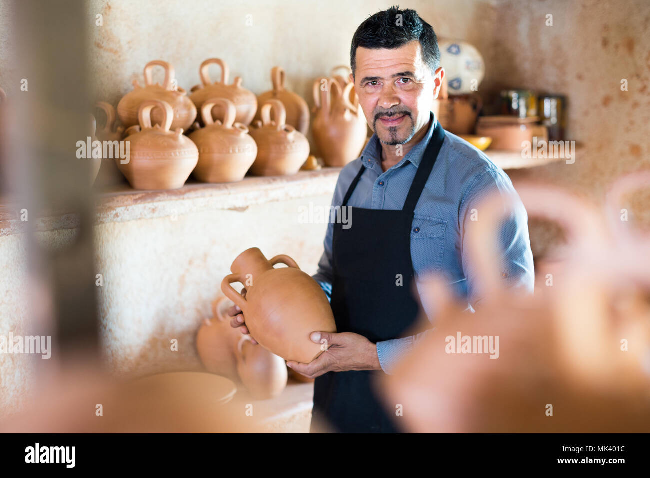 Cheerful man sculptor having ceramics in hands and standing in pottery ...