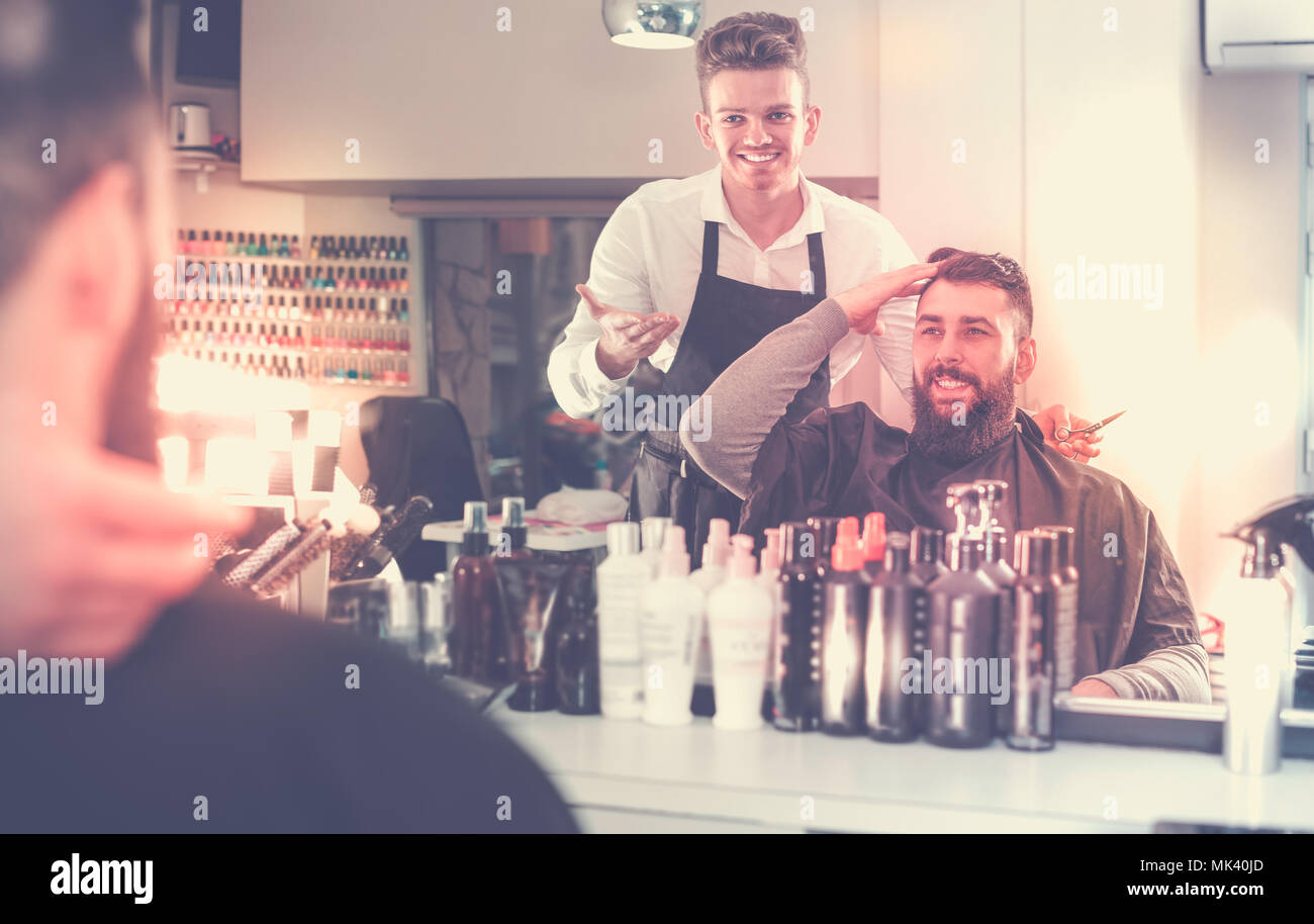 Cheerful client describing his desirable haircut to hairdresser at hair ...