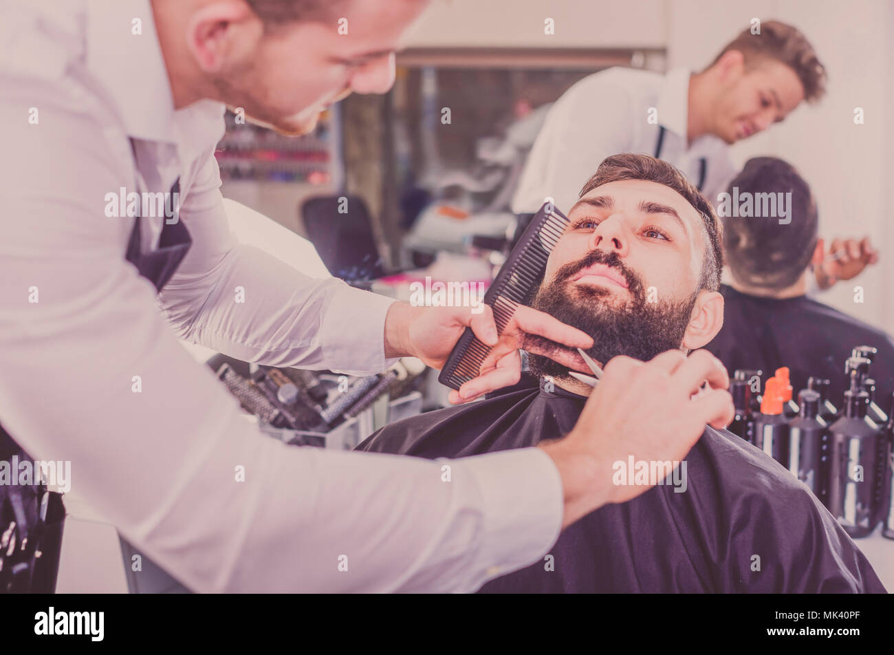 Adult guy stylist creating new shape for beard of client at ...