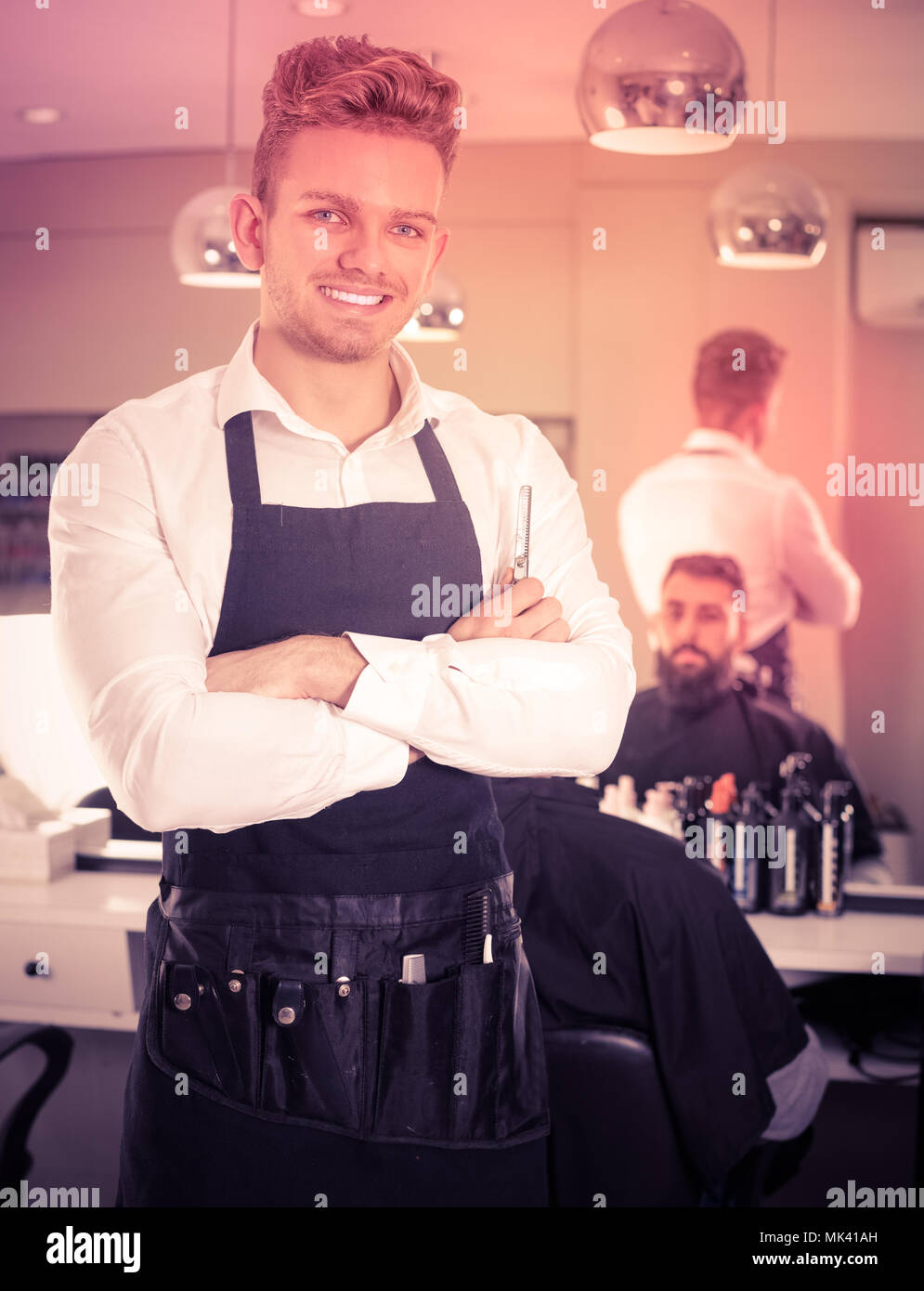 Smiling young man hairdresser demonstrating his workplace and tools at ...