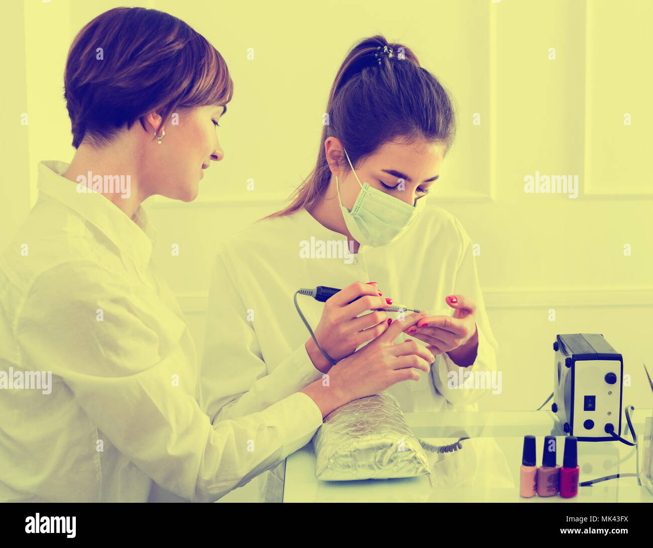 Young satisfied pleasant female client doing nails in shellac technique ...