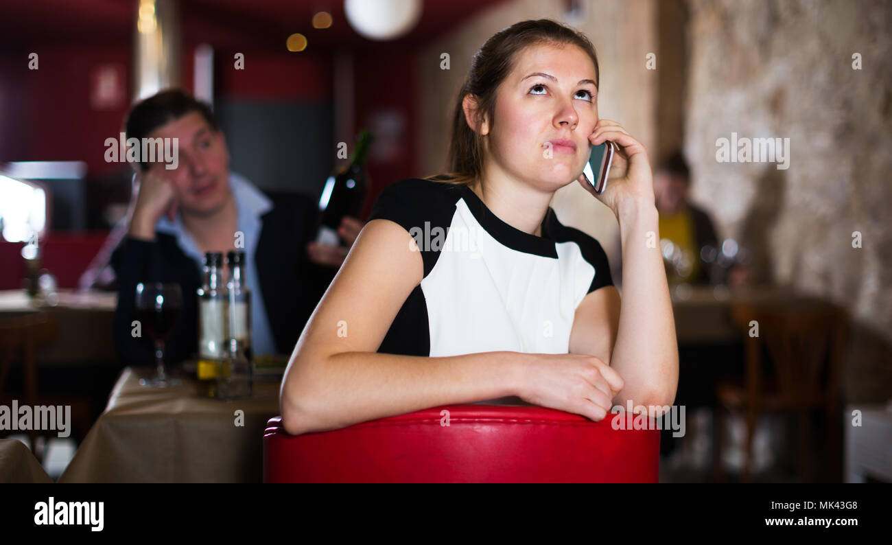 Unhappy woman talking on mobile phone sitting apart in restaurant with ...